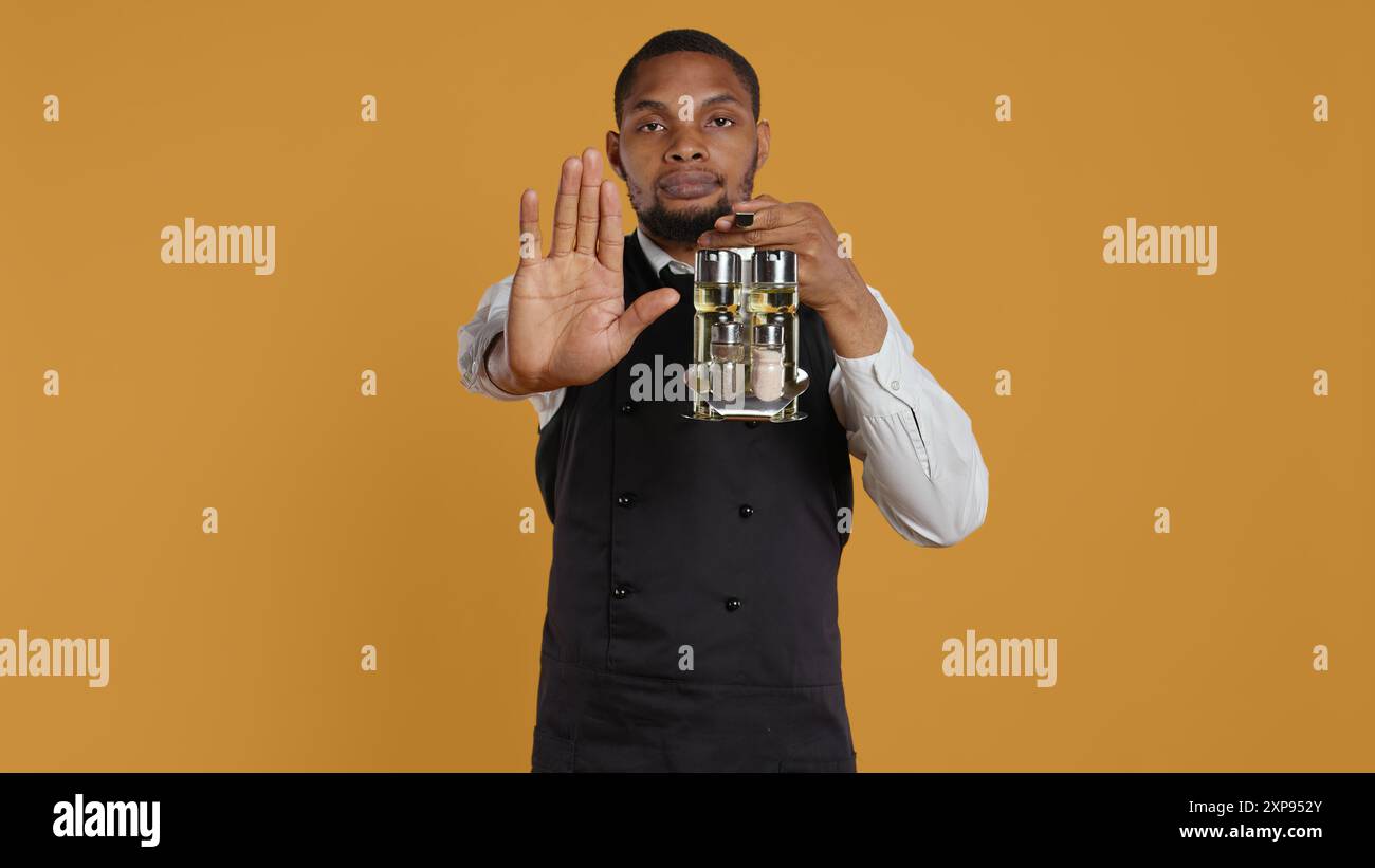 Waiter in uniform showing a stop sign with his palm raised in studio ...