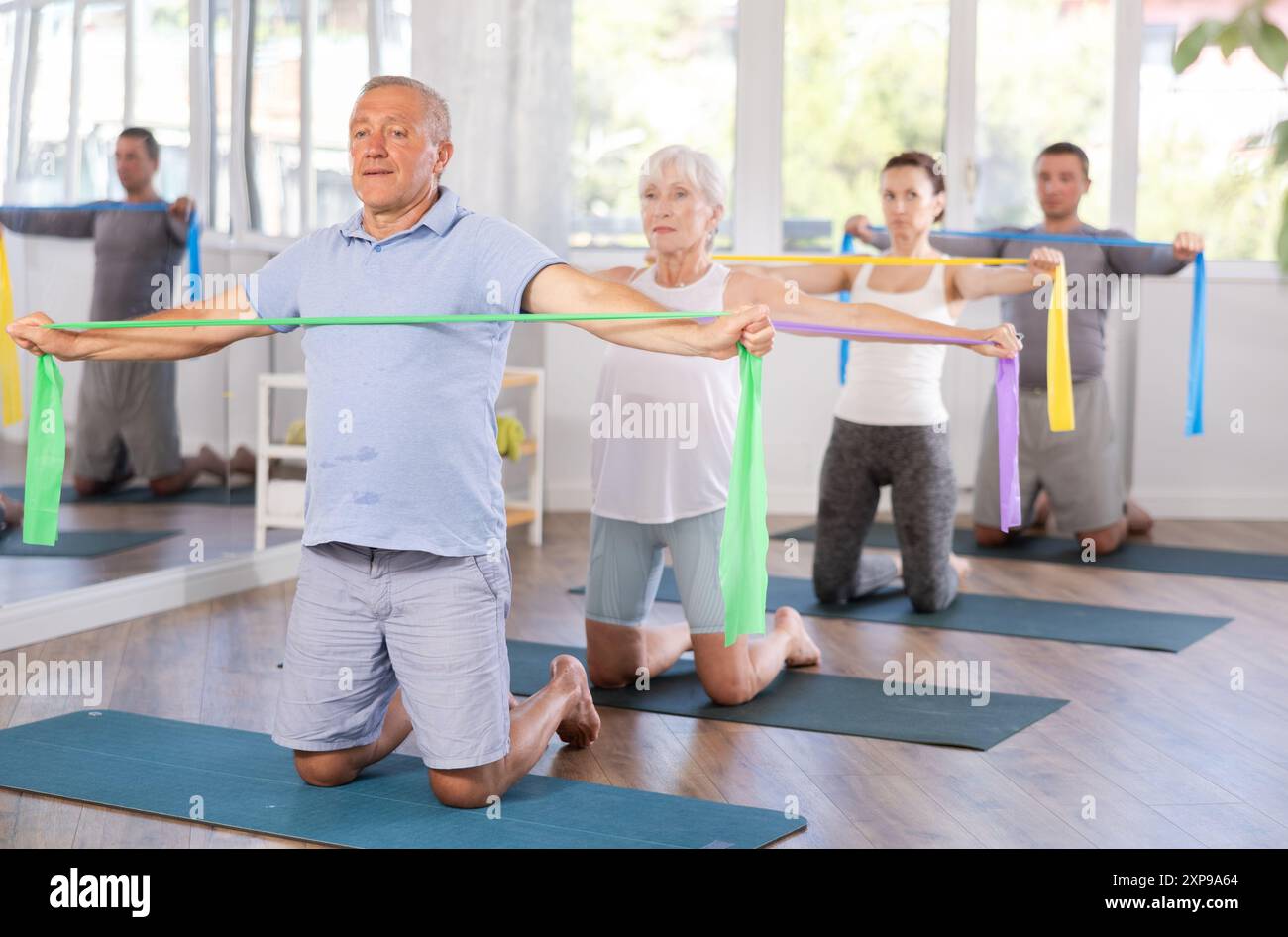 Elderly man kneeling performs exercises with wide elastic band during ...