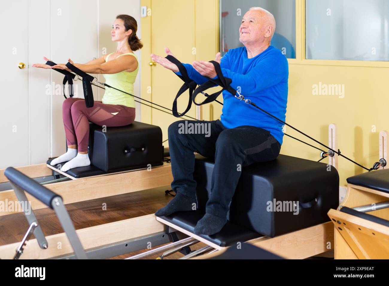 Mature man practicing Pilates system on reformer supervised in sport ...