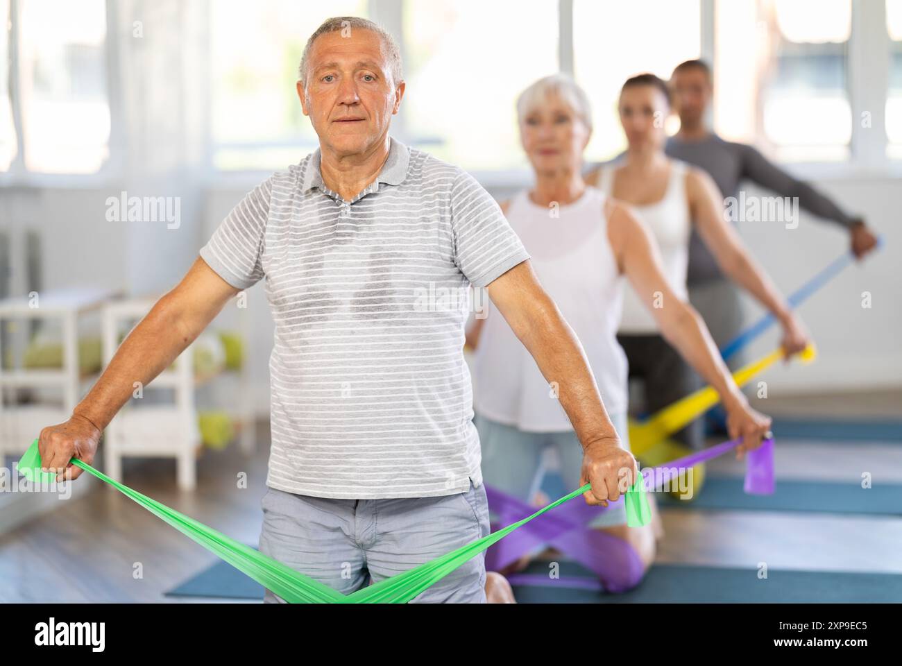Elderly man performs exercises with elastic rubber band during Pilates ...