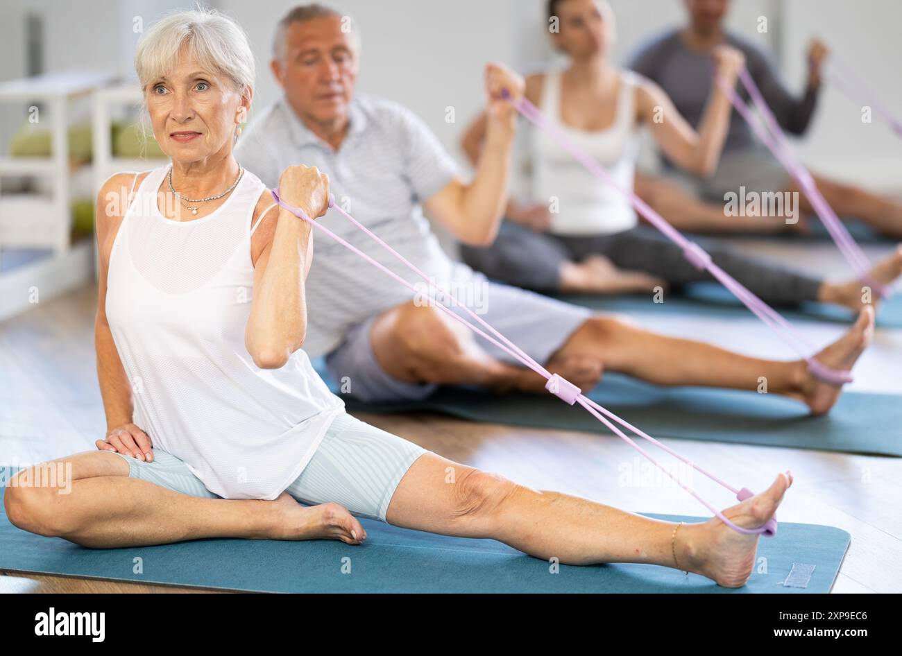 Elderly woman performs stretches elastic band with hand and foot while ...