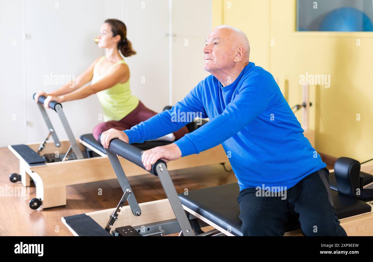 Elderly man performing pilates exercises on reformer during group ...