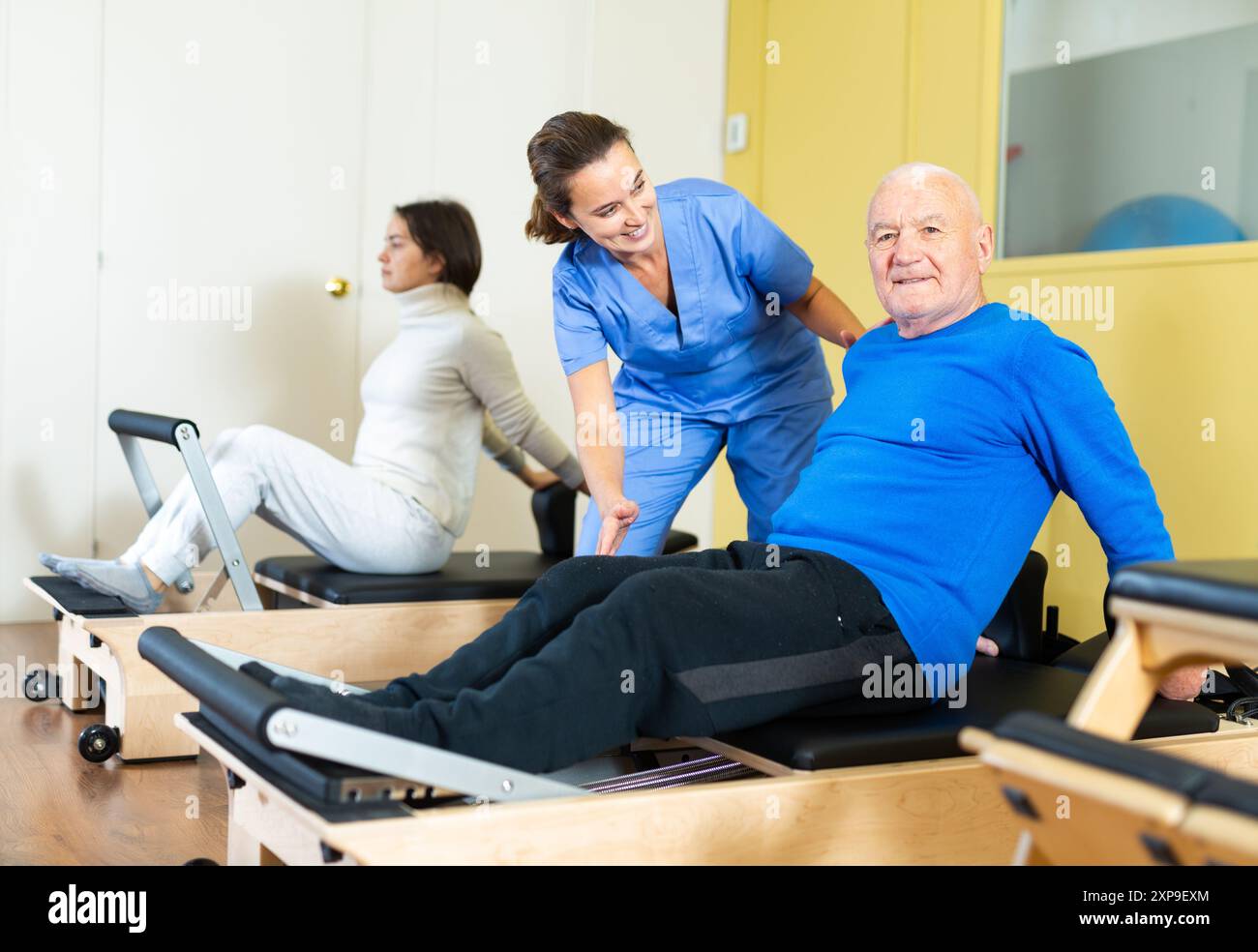 Rehabilitation physician controlling senior man exercising on pilates ...