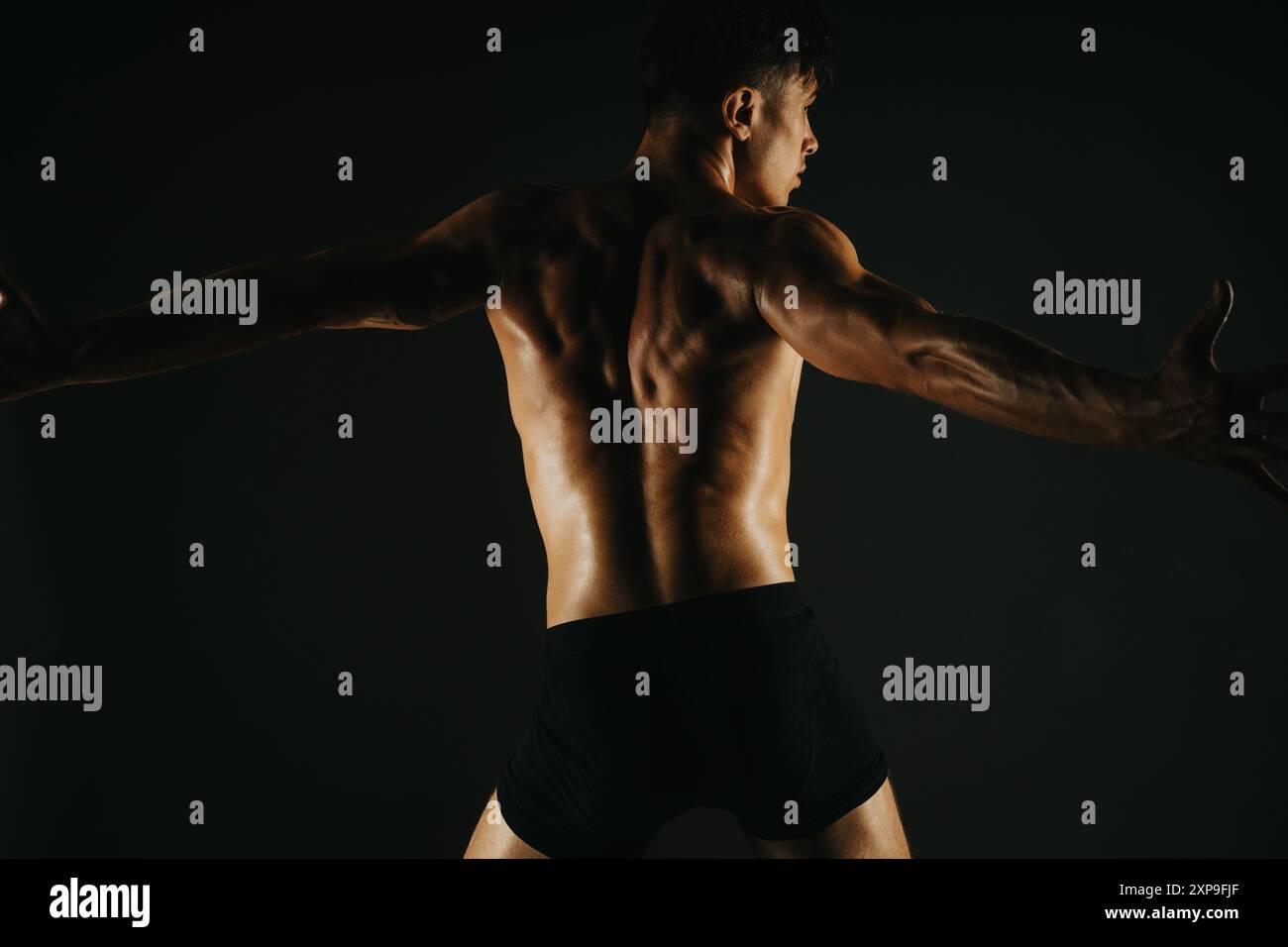 Fit man showing his back muscles in a dark studio setting showcasing ...