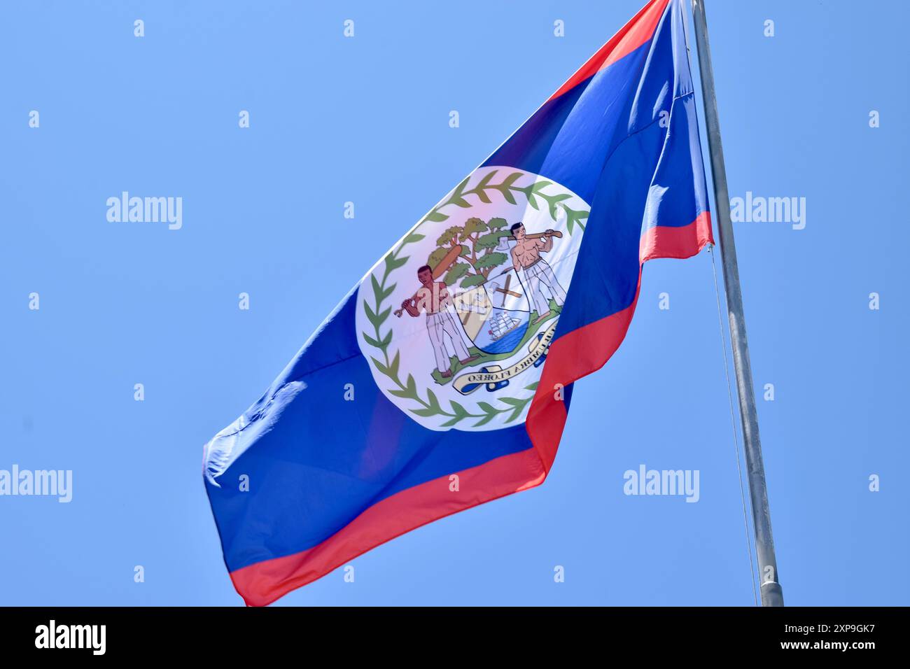 The Belize flag floating in the wind against a clear blue sky ...