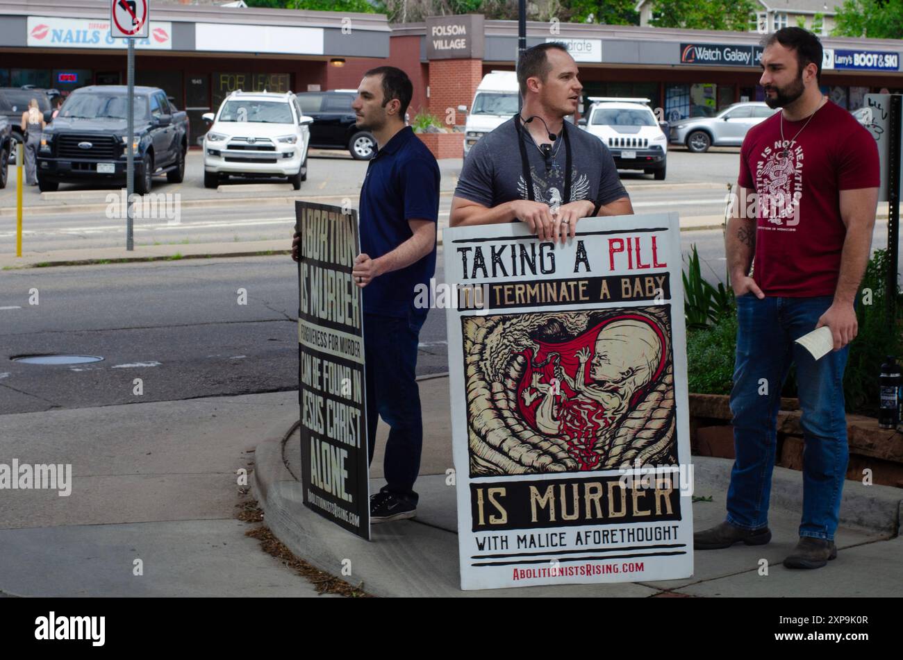 Three men with signs bearing anti-abortion messages stand on a sidewalk ...