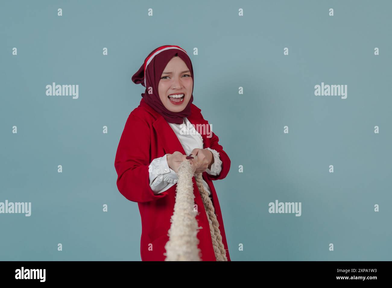 Young Indonesian woman in a red jacket and hijab is pulling on a rope ...
