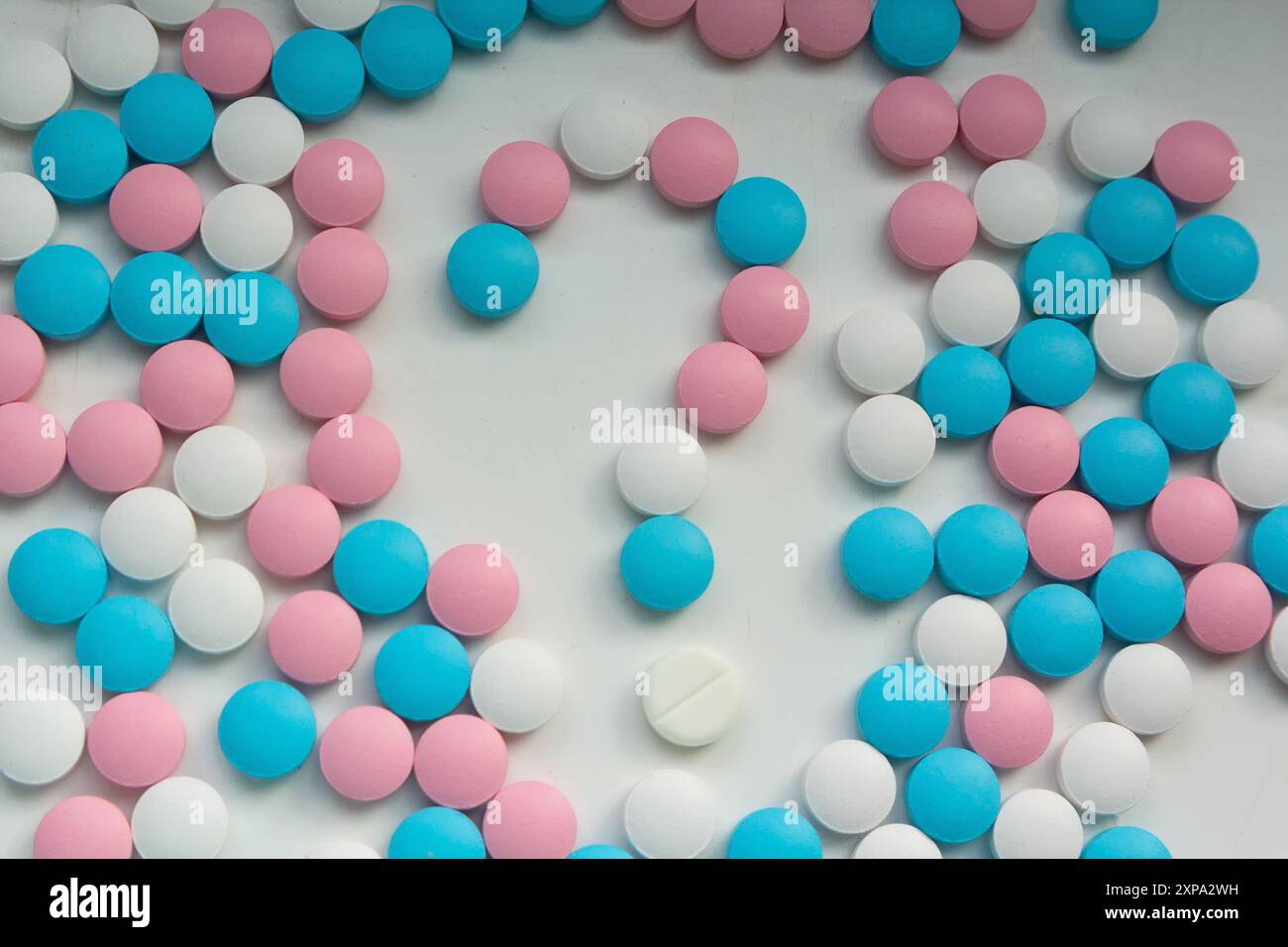 White, blue and pink pills in the shape of a question mark are ...