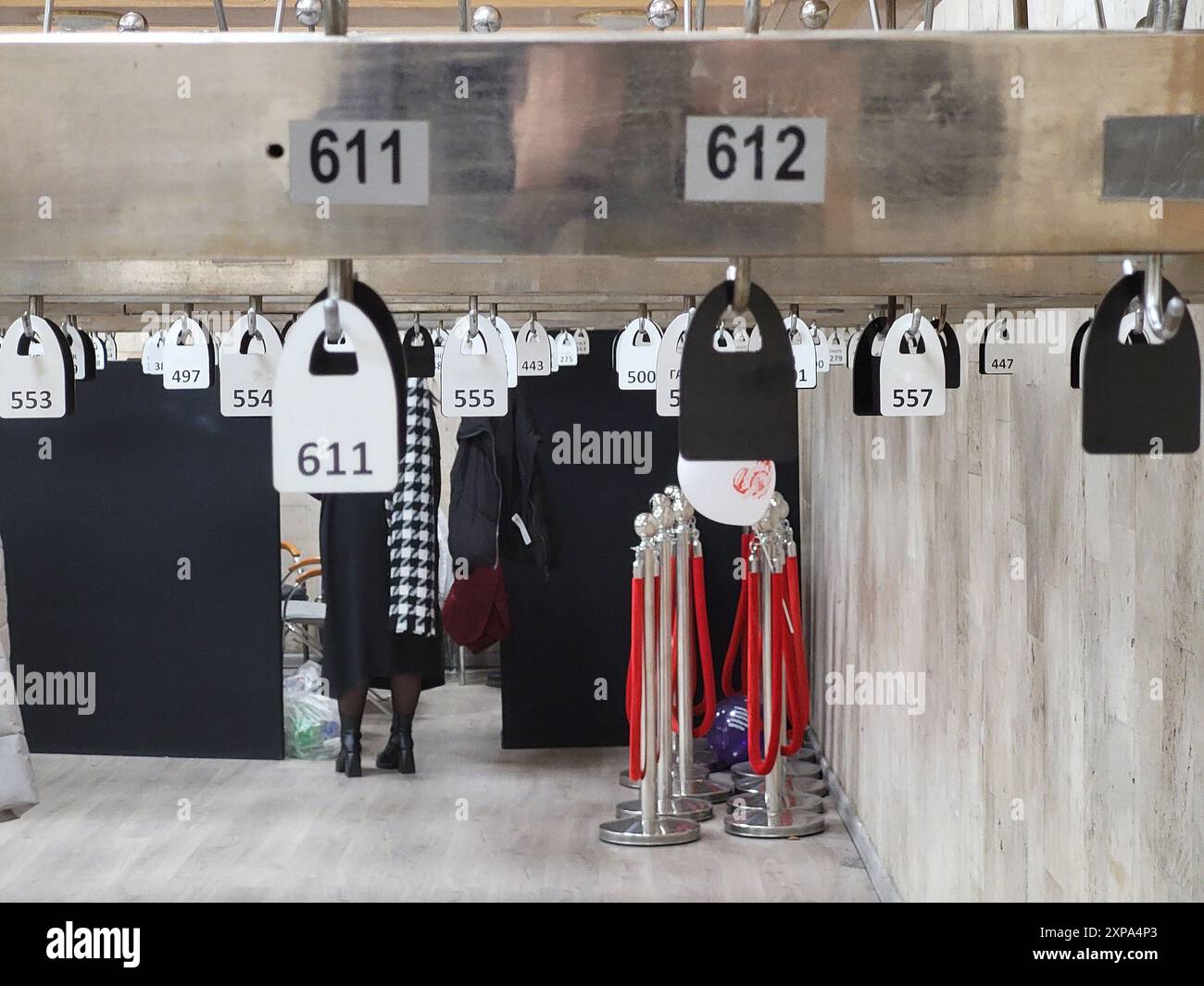 Coat check area with numbered tags hanging from metal racks. Person ...