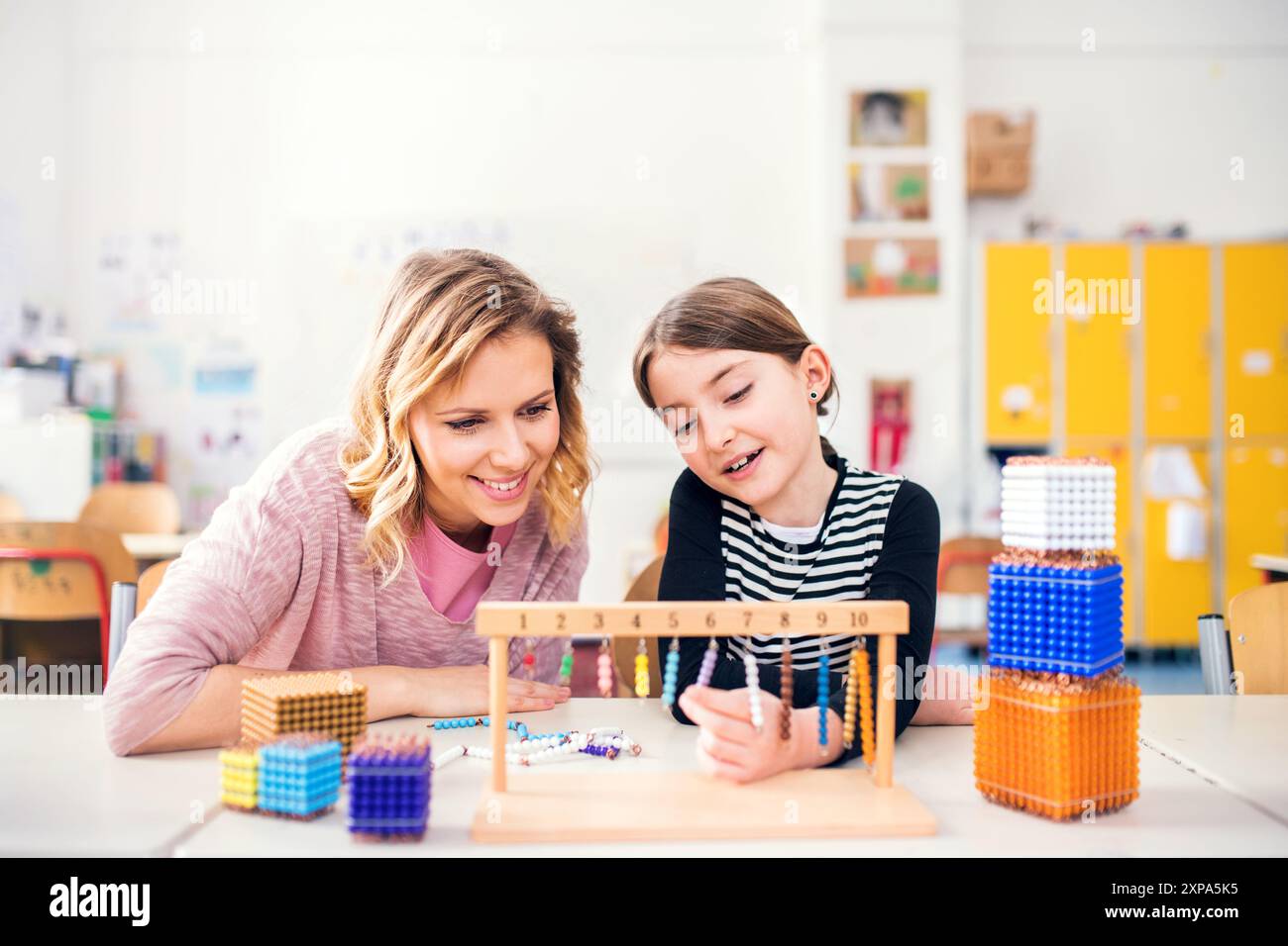 Hardworking teacher learning with young schoolgirl in classroom ...