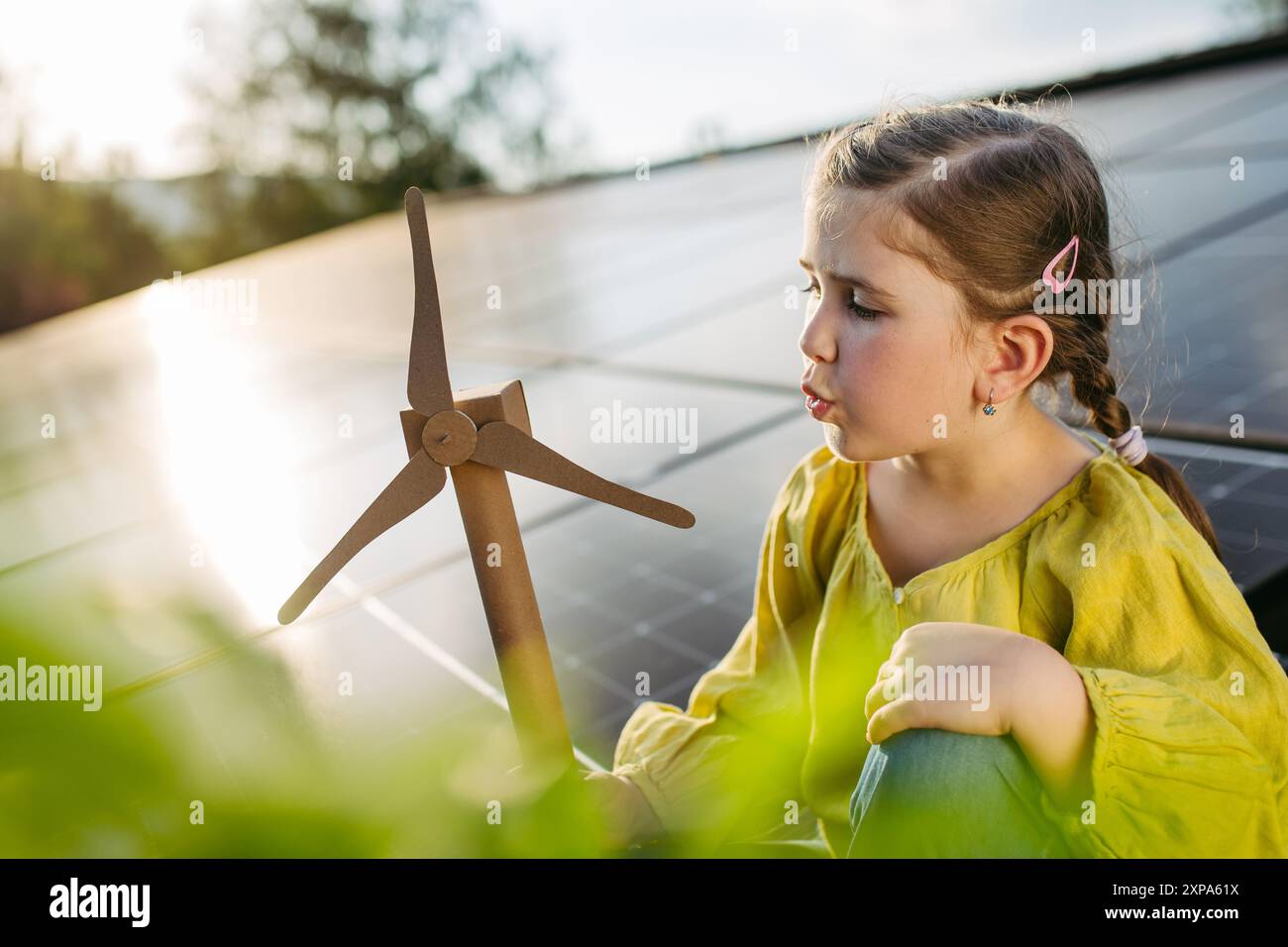 Cute girl on roof with solar panels, blowing into model of wind turbine ...