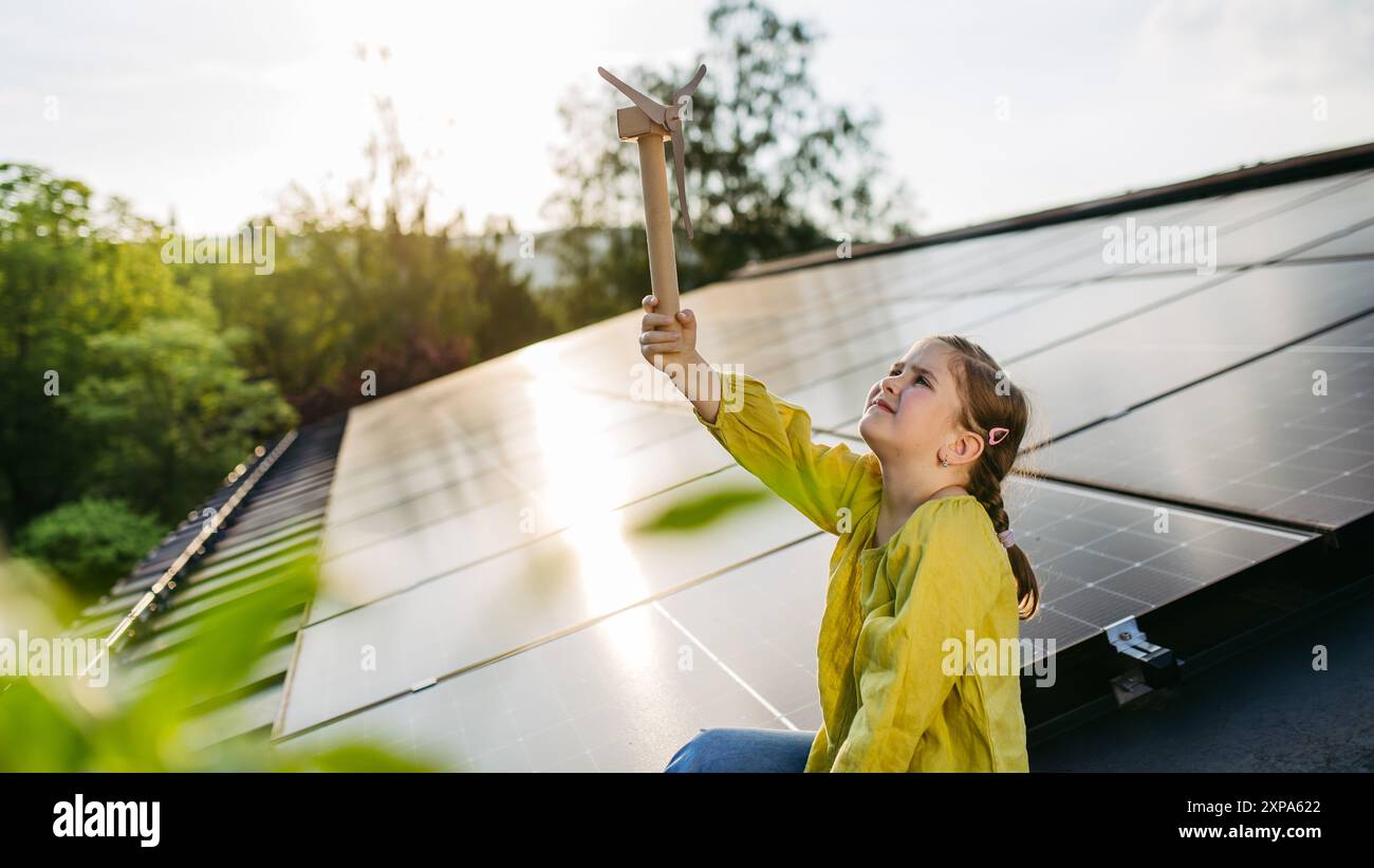 Cute girl on roof with solar panels, holding model of wind turbine ...