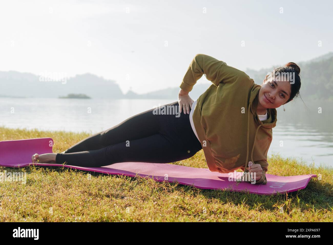 Beautiful young Asian woman is laying on a mat in a grassy field, doing ...