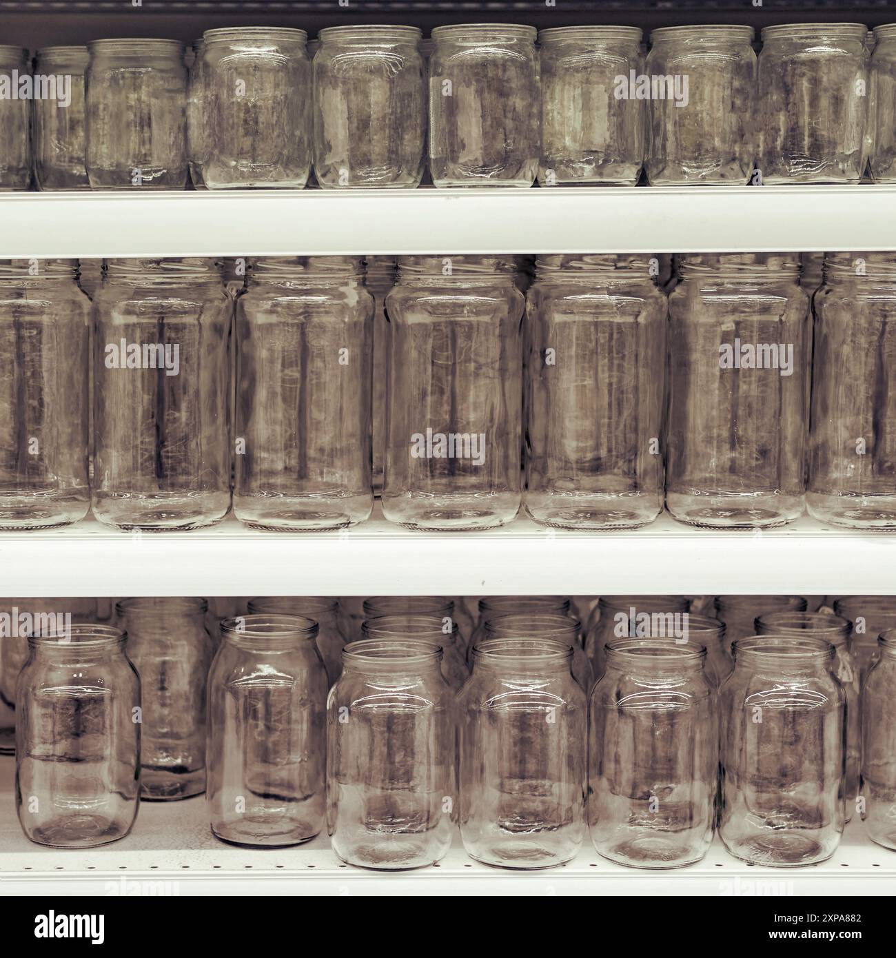 Empty glass jars arranged on white shelves. Shelf display of glass ...