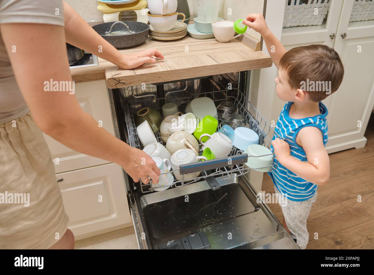 A mother woman and child unload a dishwasher in a home kitchen. Baby ...