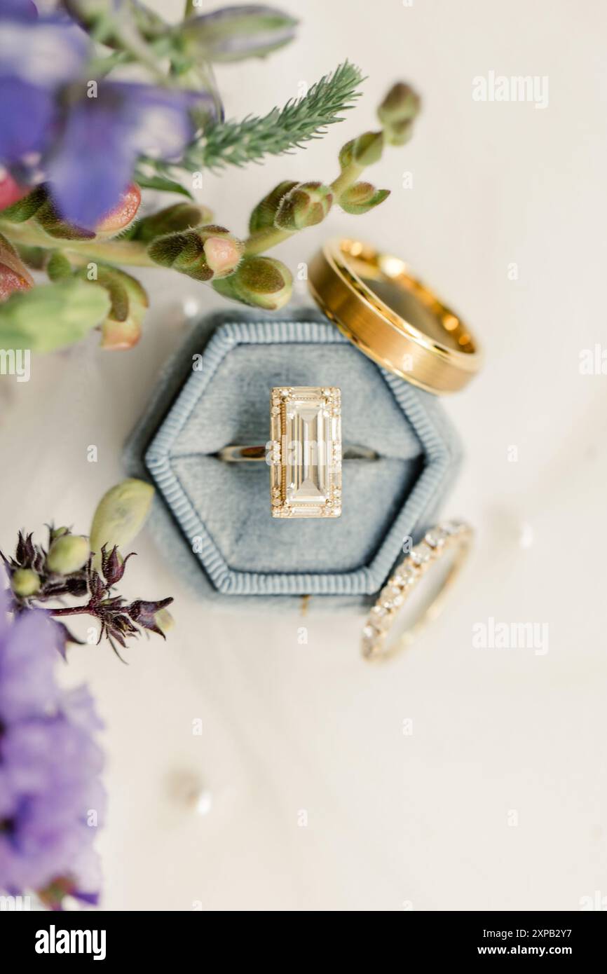 Gold wedding rings and an emerald-cut engagement ring in a blue box ...