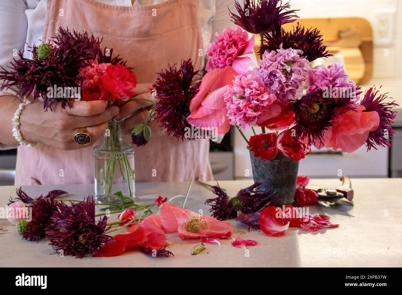 Woman arranging a bouquet of poppies in a vase on a kitchen counter ...