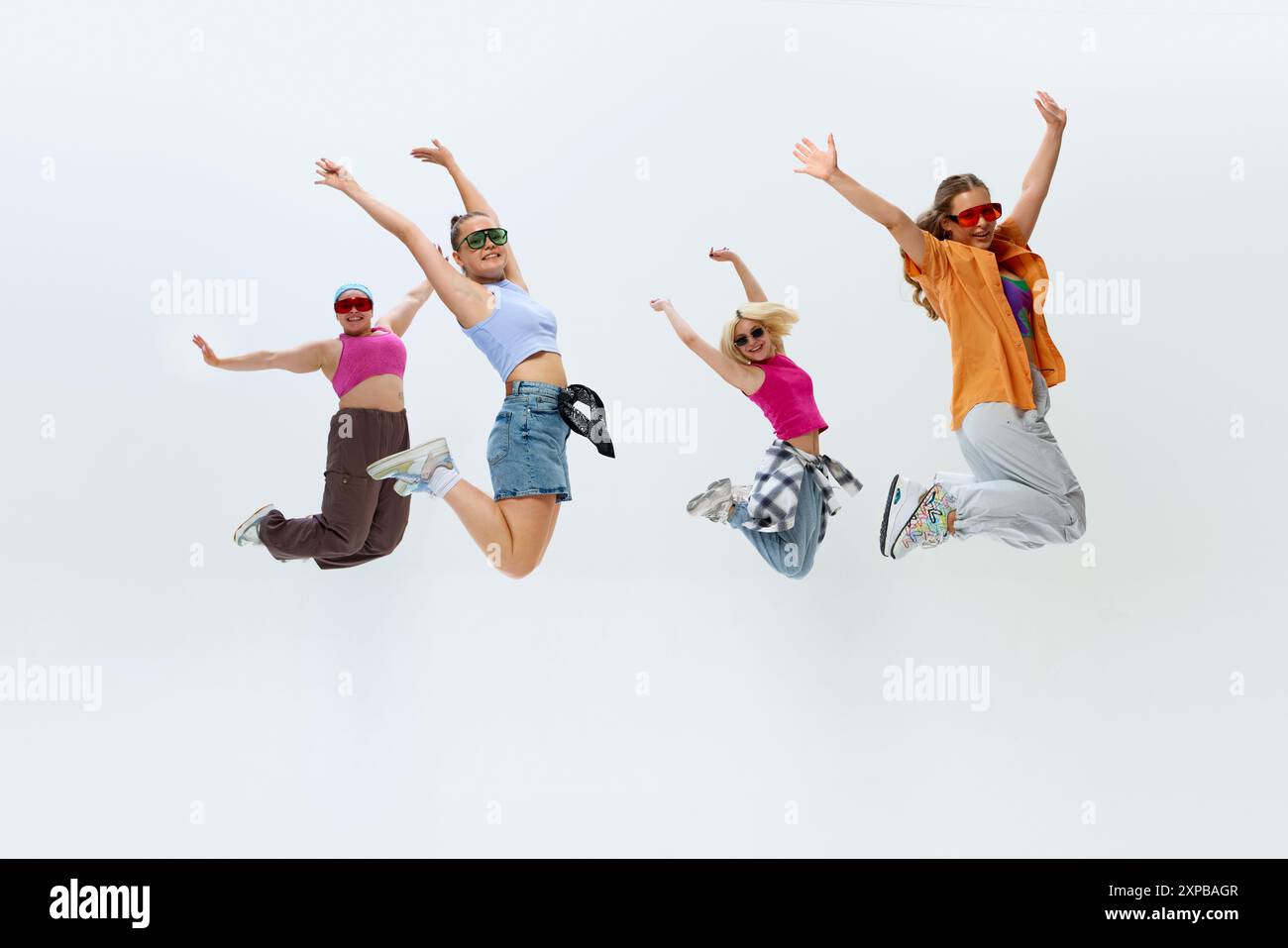 Four friends, dressed in stylish, colorful attire and sunglasses, show ...