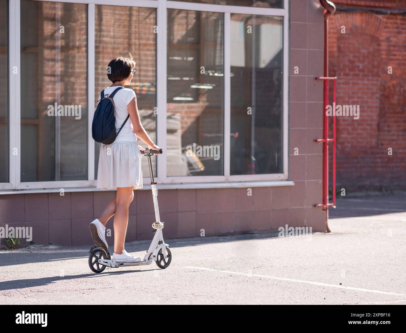 Young woman rides kick scooter down the street at sunset. Eco-friendly ...