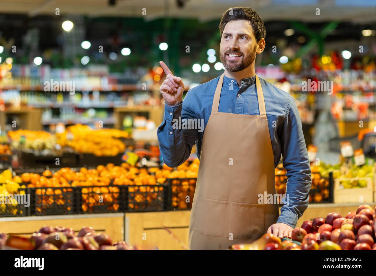 Smiling grocery store worker standing in produce section pointing at ...