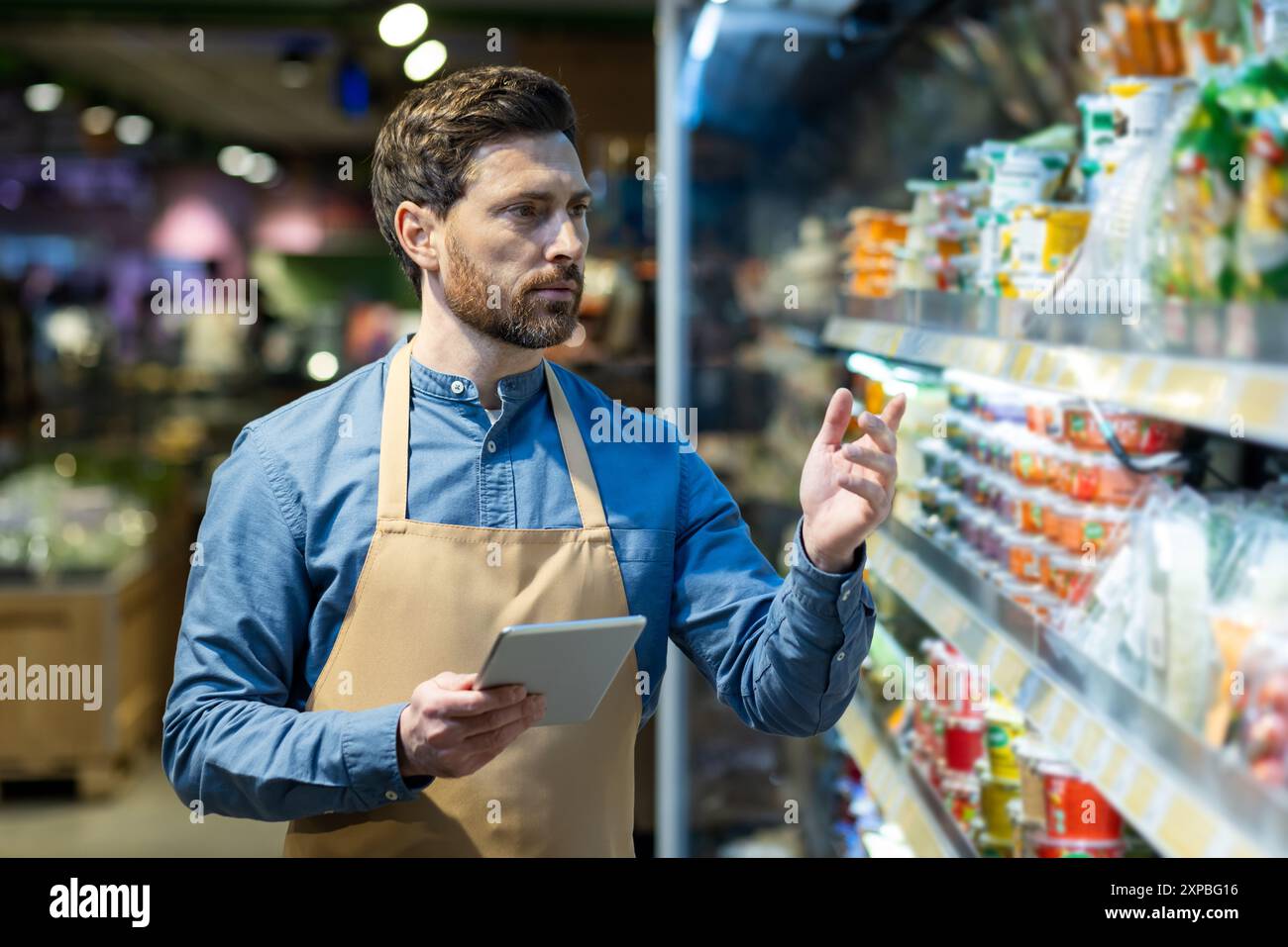 Supermarket employee checking products on shelves while holding tablet ...
