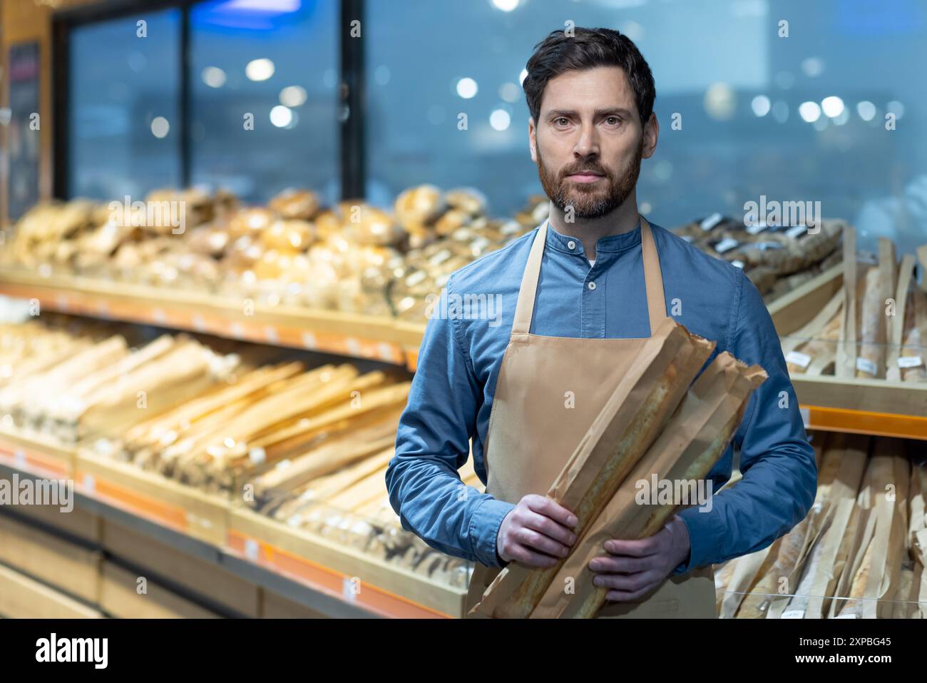 Baker holding fresh baguettes in front of supermarket bread section ...