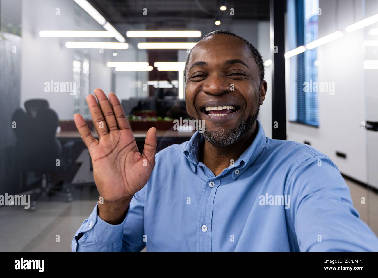 Smiling businessman waving and engaging in friendly phone video call in ...