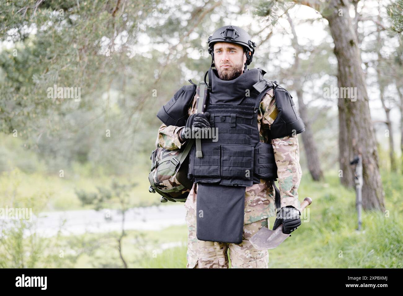 Young soldier in uniforms and tactical vest works in the forest and ...