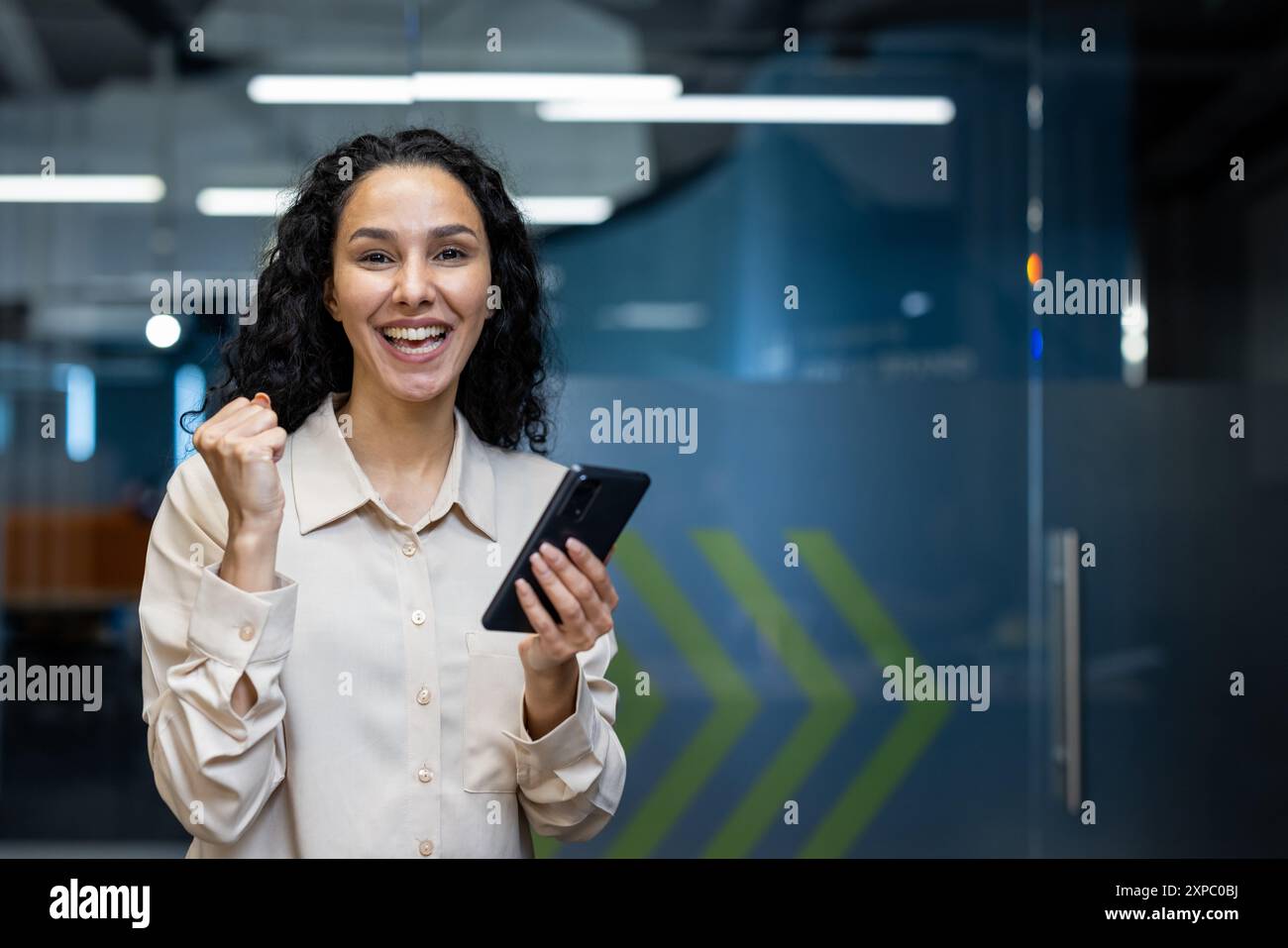 Joyful businesswoman in modern office celebrating success with phone in ...