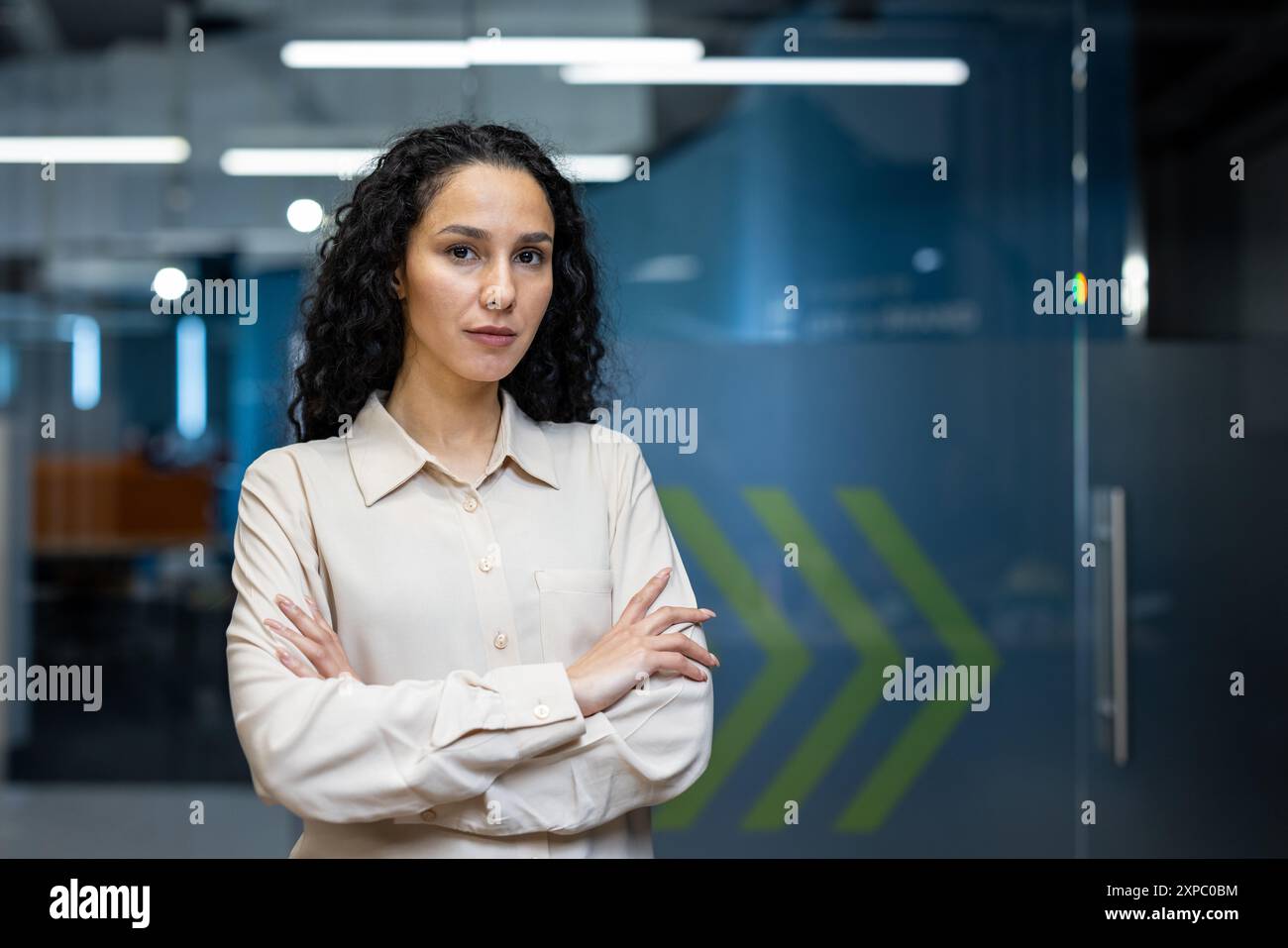 Confident businesswoman standing with arms crossed in modern office ...