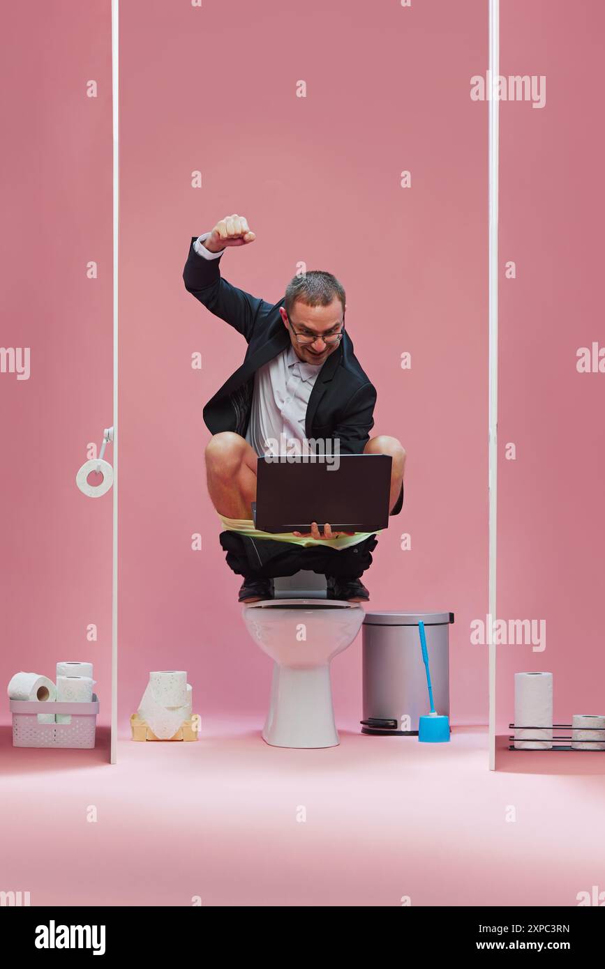 Emotional businessman sitting atop of toilet with laptop and watching ...