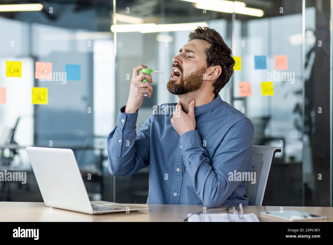 Businessman sitting at desk in modern office using throat spray. Man ...