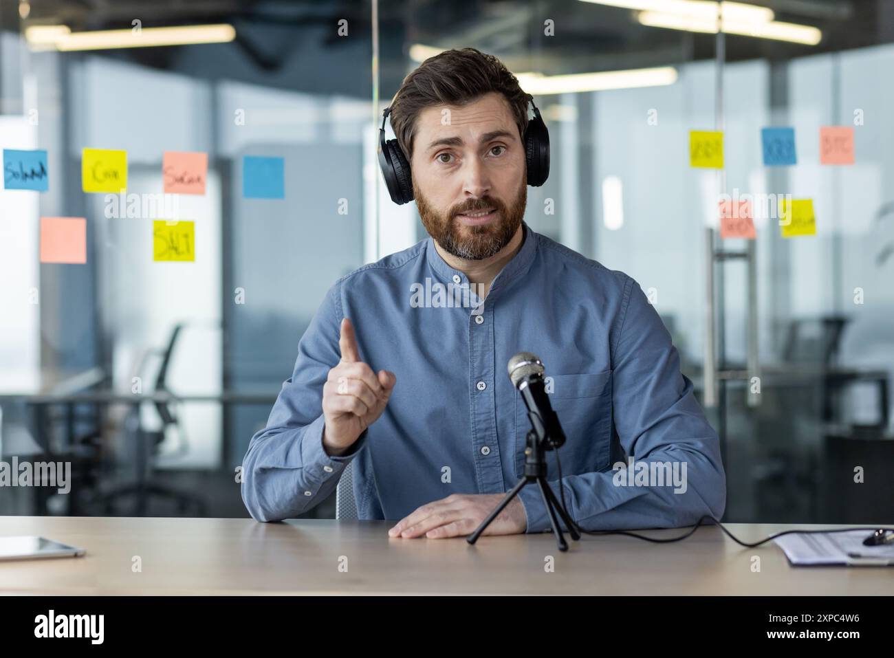 Confident man wearing headphones and recording podcast in office ...