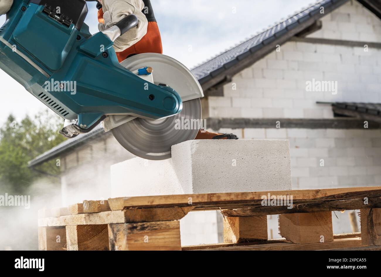 A worker uses a power tool to cut concrete blocks on wooden pallets at a construction site under ...