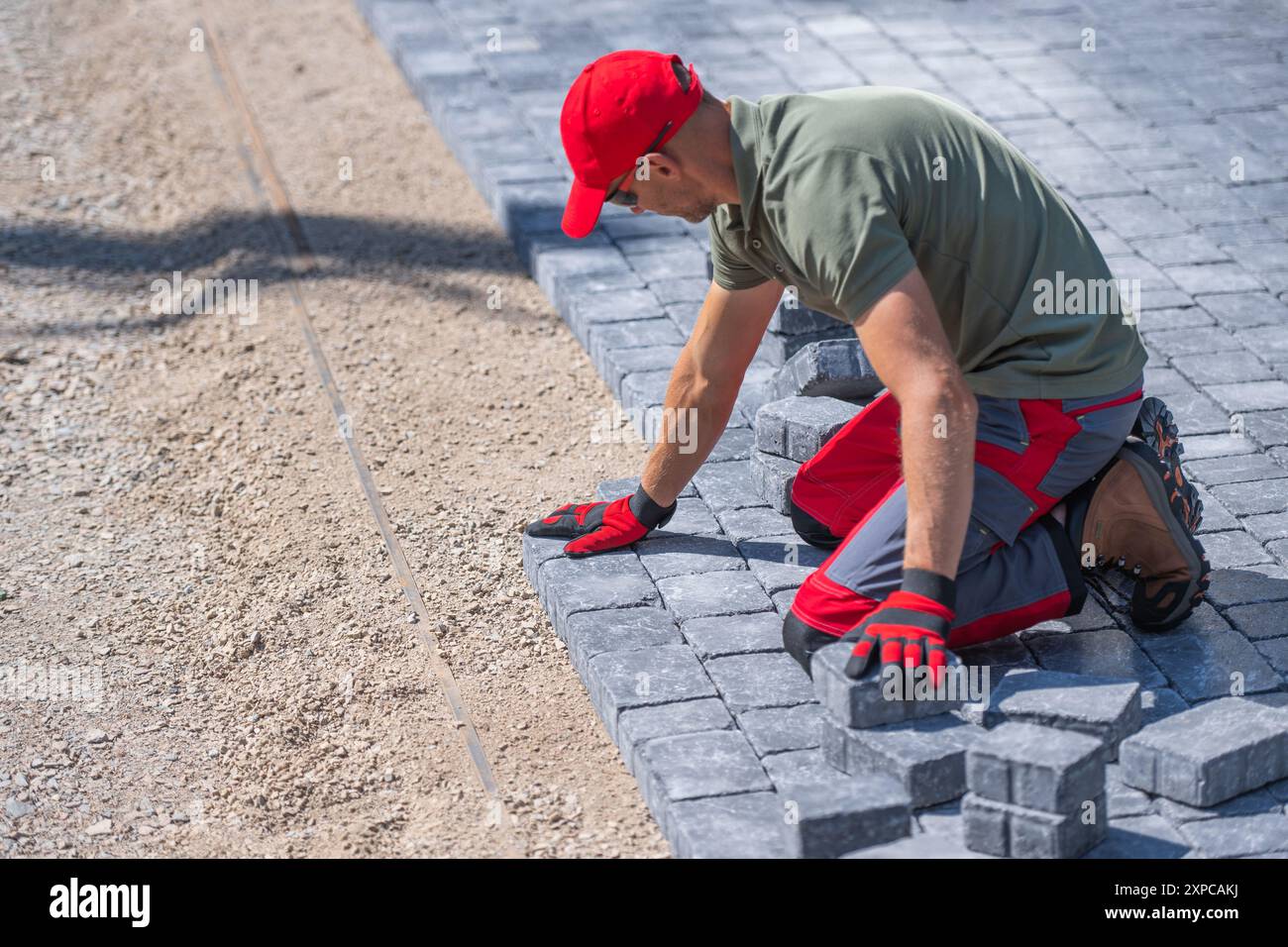 A worker is carefully laying down pavers on a prepared gravel base ...