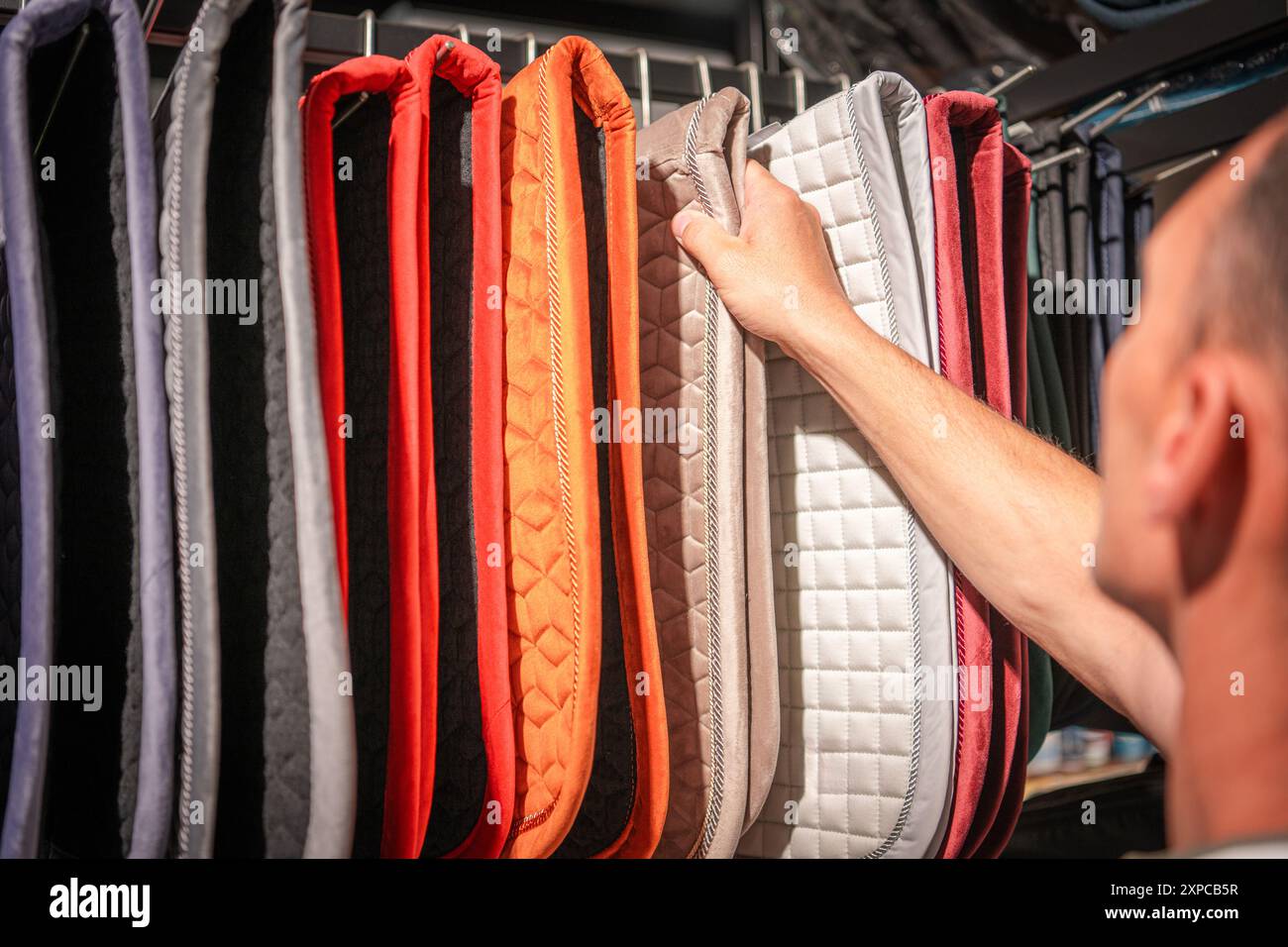 A hand reaches for a colorful assortment of saddle pads displayed in a ...