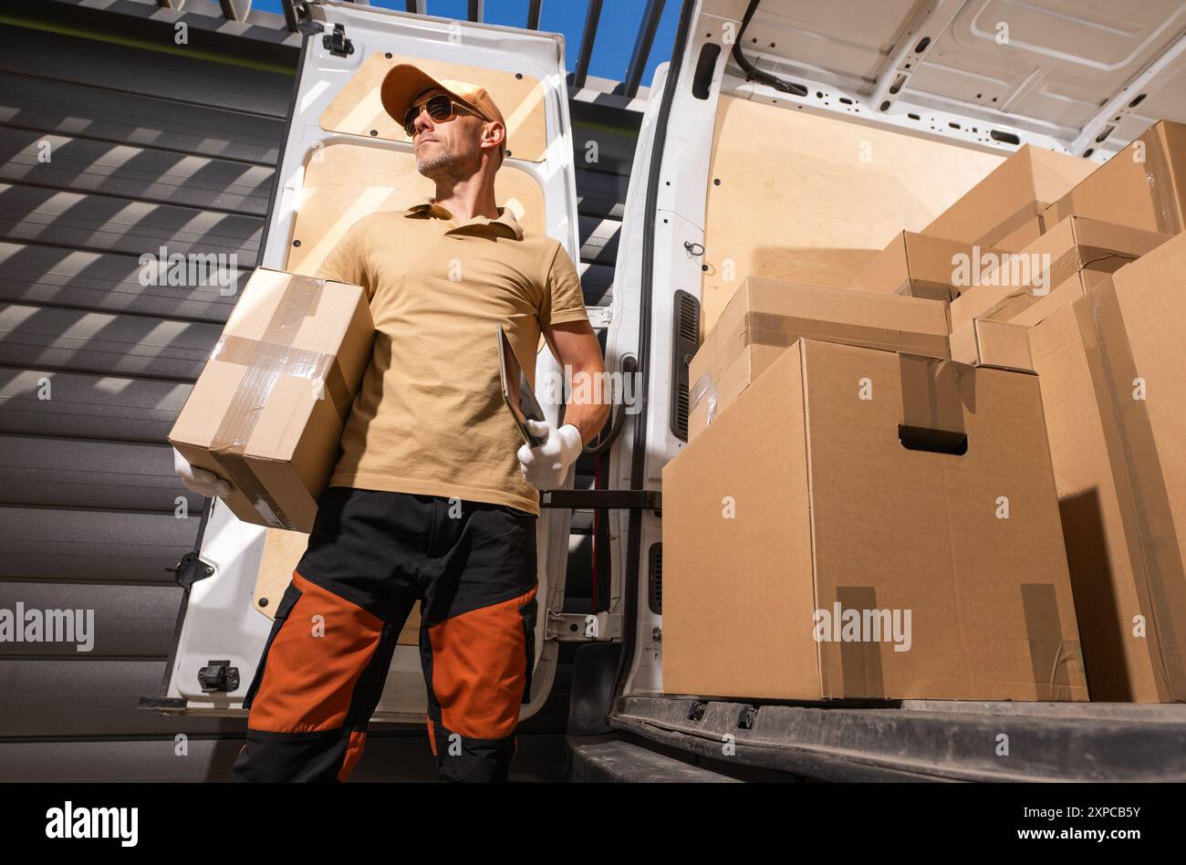 A delivery person stands confidently at the back of a van, holding ...