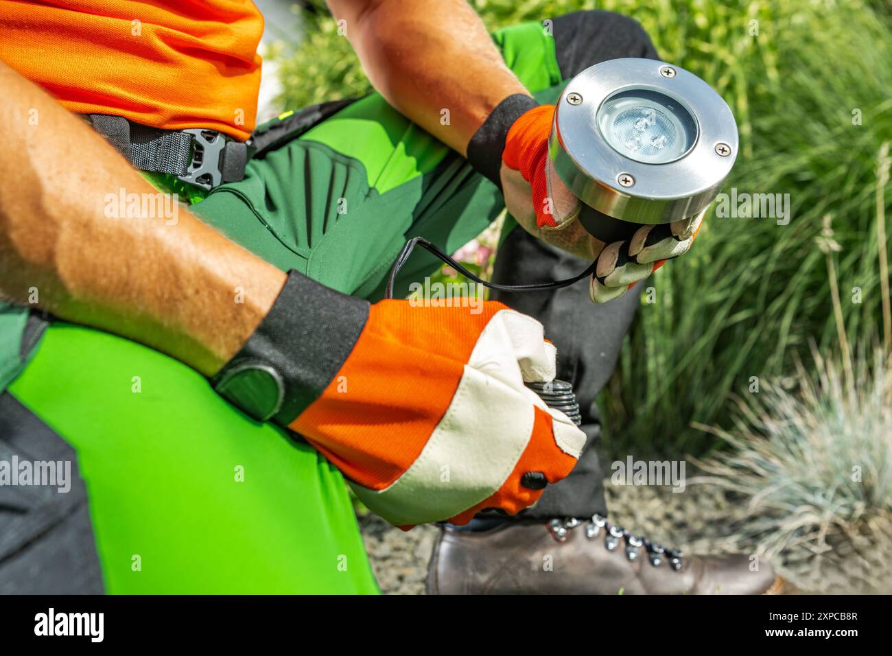 A gardener in bright attire prepares to install an outdoor light ...