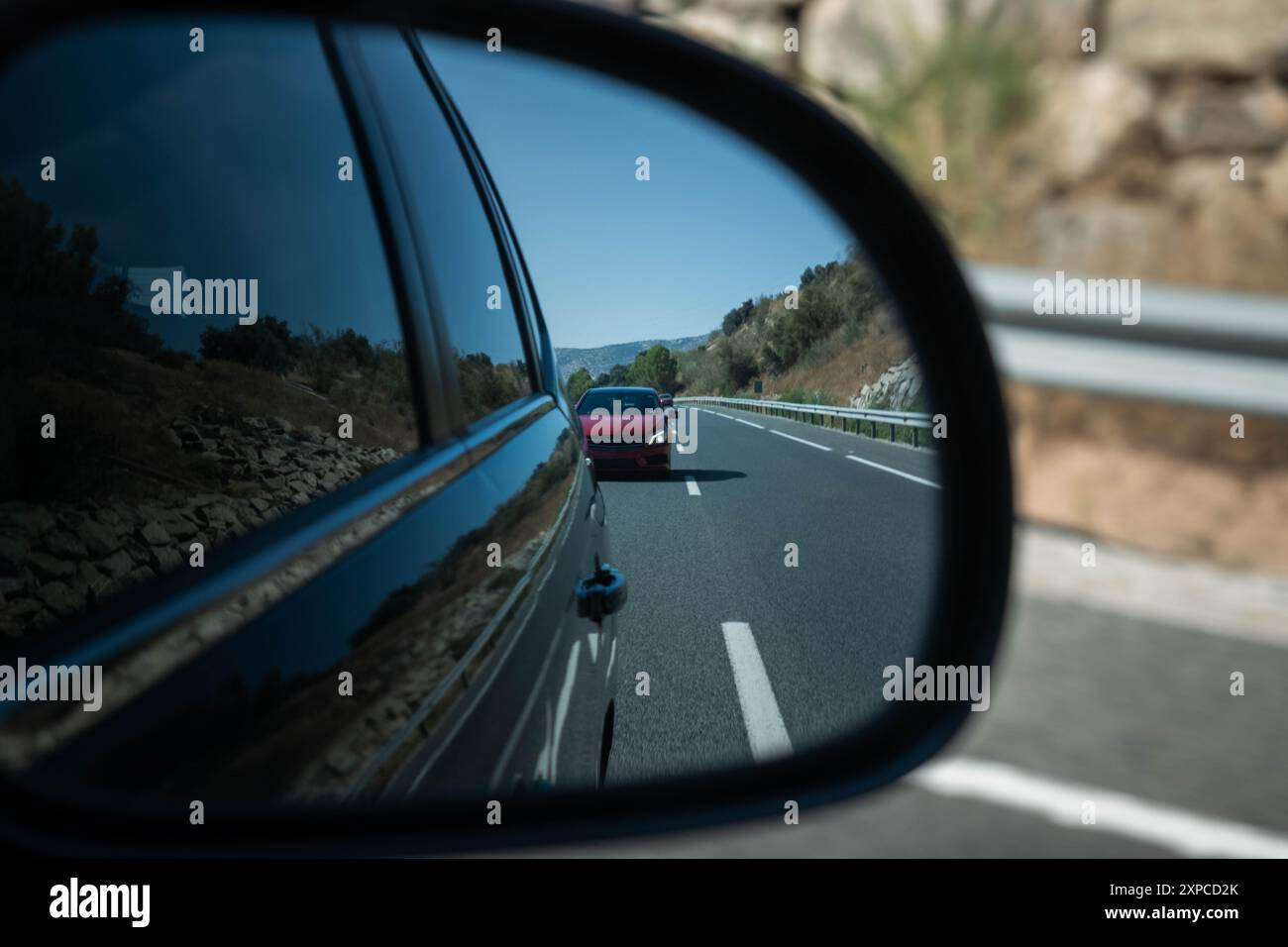 A red car approaches from behind through the right rearview mirror of a ...