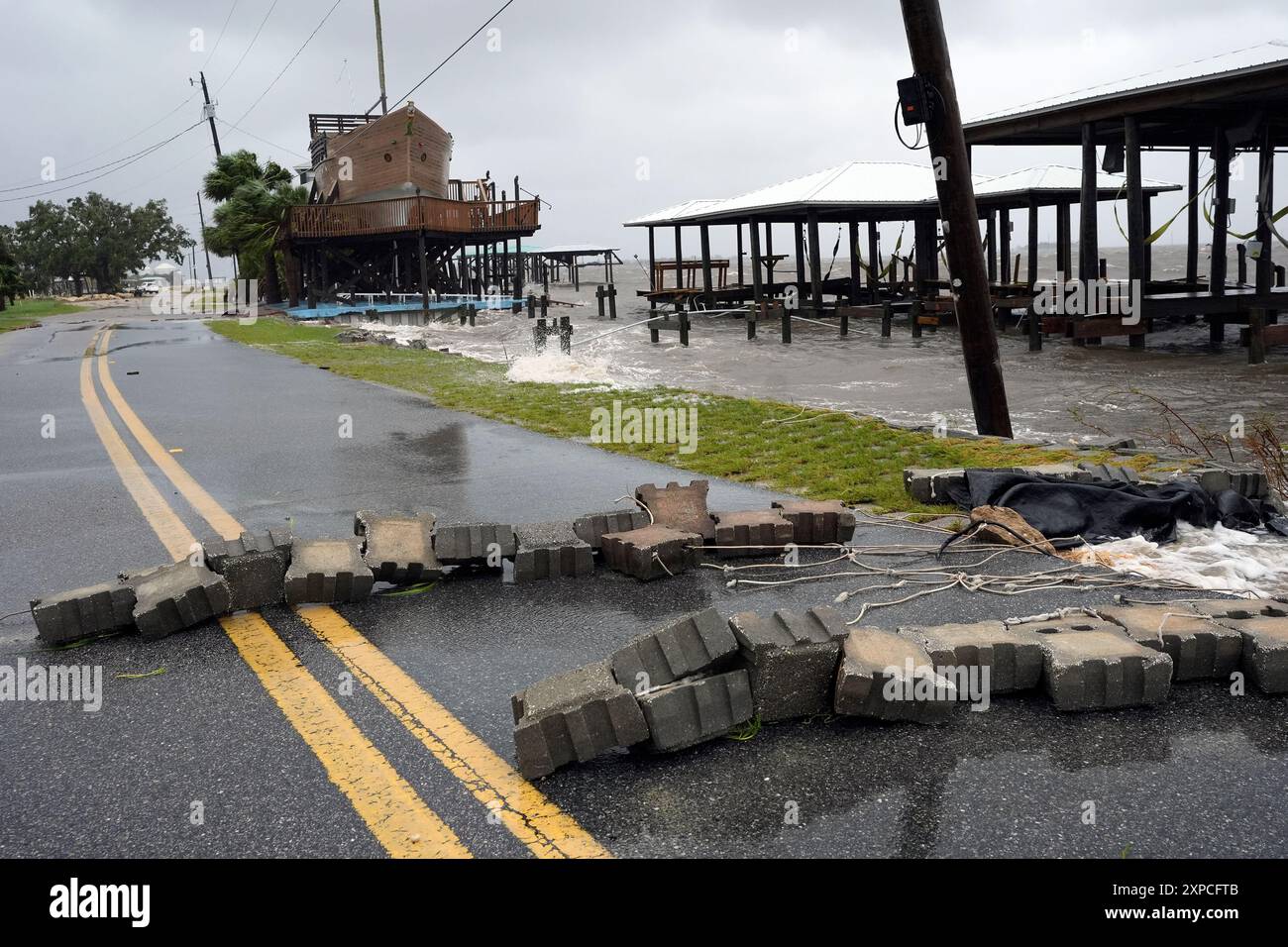 A block wall, knocked over from storm surge, blocks a road near homes ...