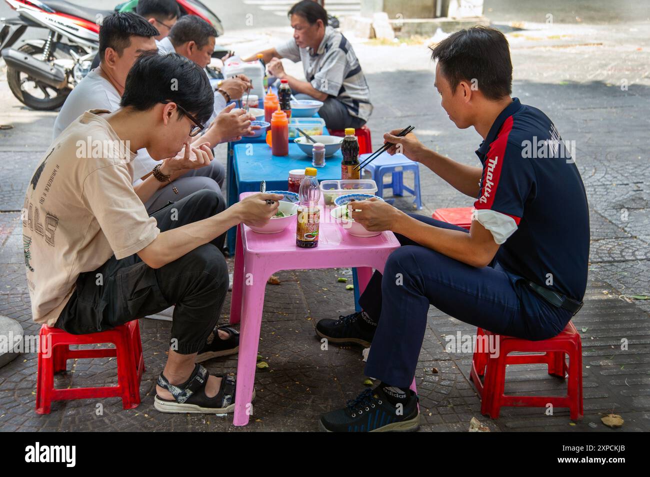 a group of Saigon office workers sit down at a mobile street food ...