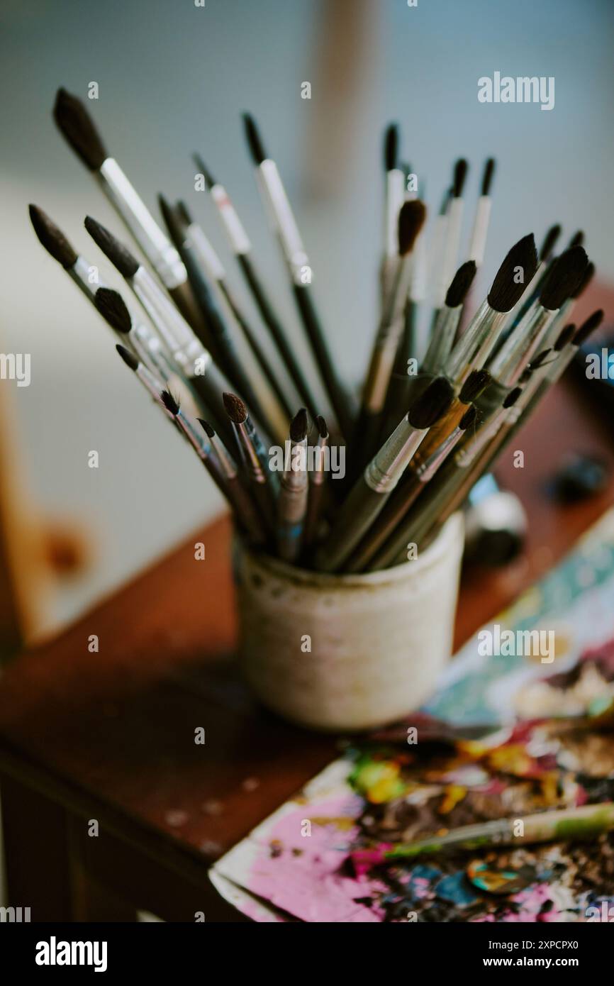 Vertical high angle closeup of bunch of paintbrushes in vessel on table ...