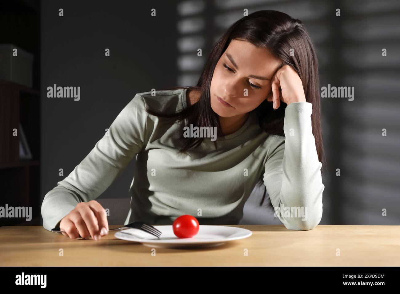 Eating disorder. Sad woman with fork near tomato at wooden table Stock ...