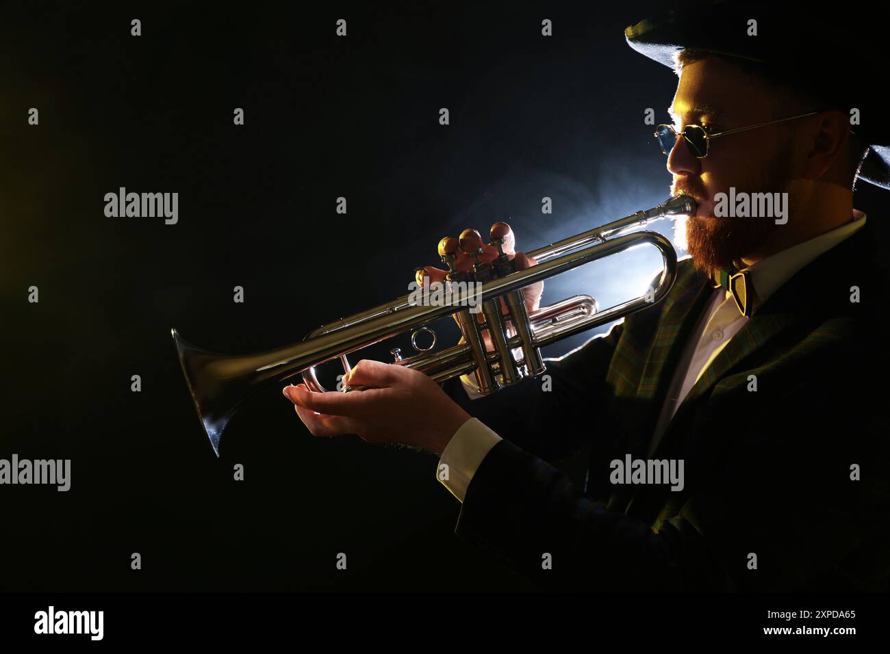 Professional musician playing trumpet on black background in smoke ...