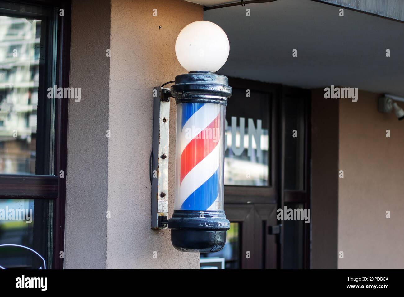 A red, white, and blue barber pole is mounted on the exterior wall of a ...