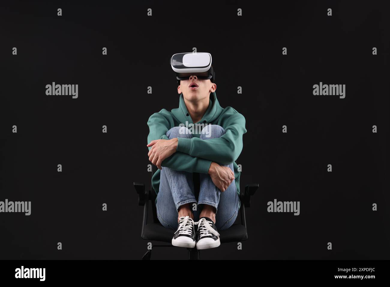 Emotional young man with virtual reality headset sitting on chair ...
