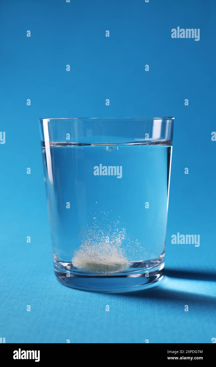 Effervescent pill dissolving in glass of water on light blue background ...