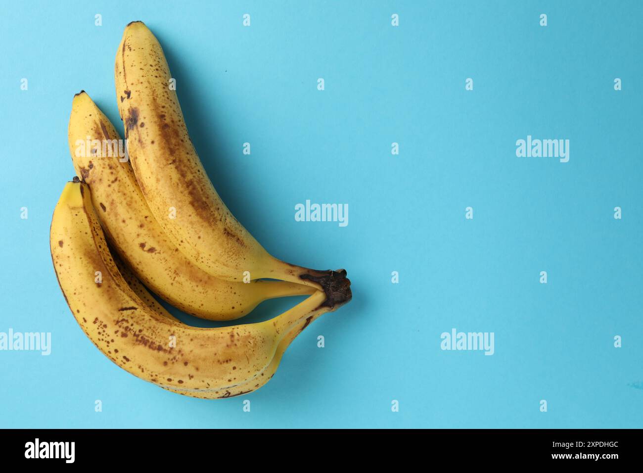 Bunch of ripe bananas with dark spots on light blue background, top ...