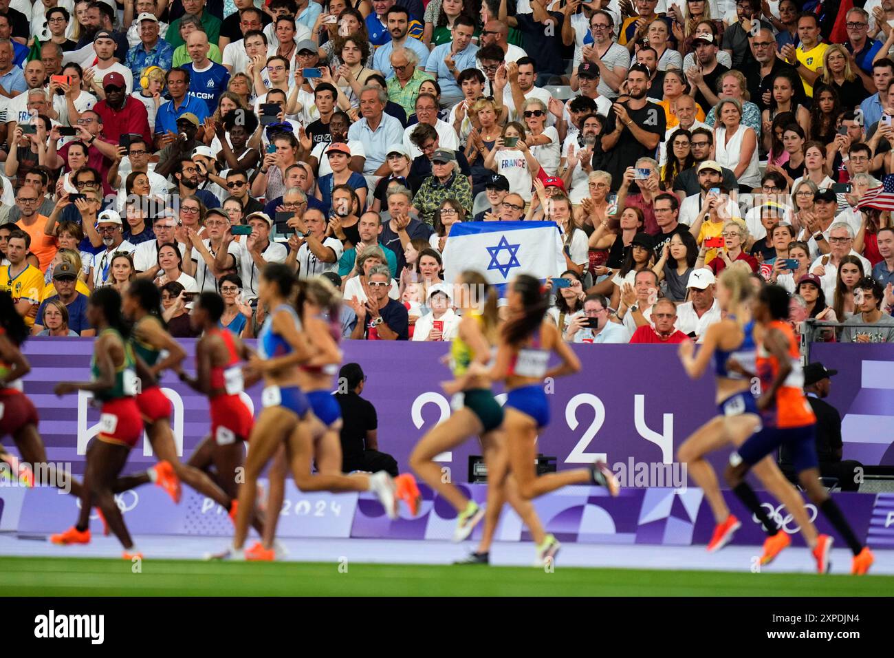 A spectator holds an Israeli national flag while watching runners ...