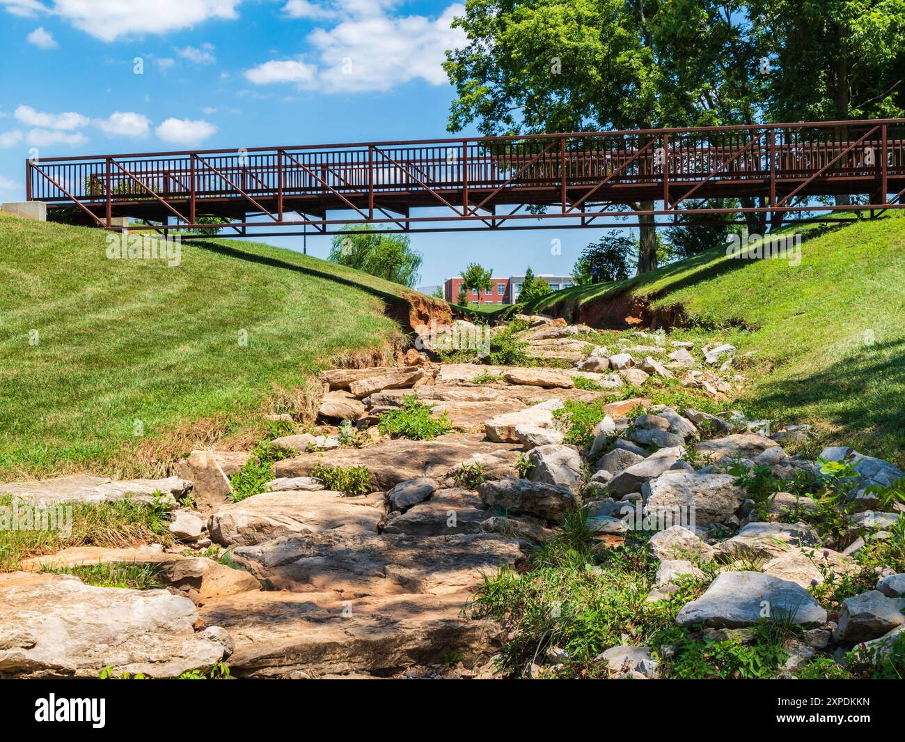 Rock lined pseudo stream under weathered steel footbridge with mown ...
